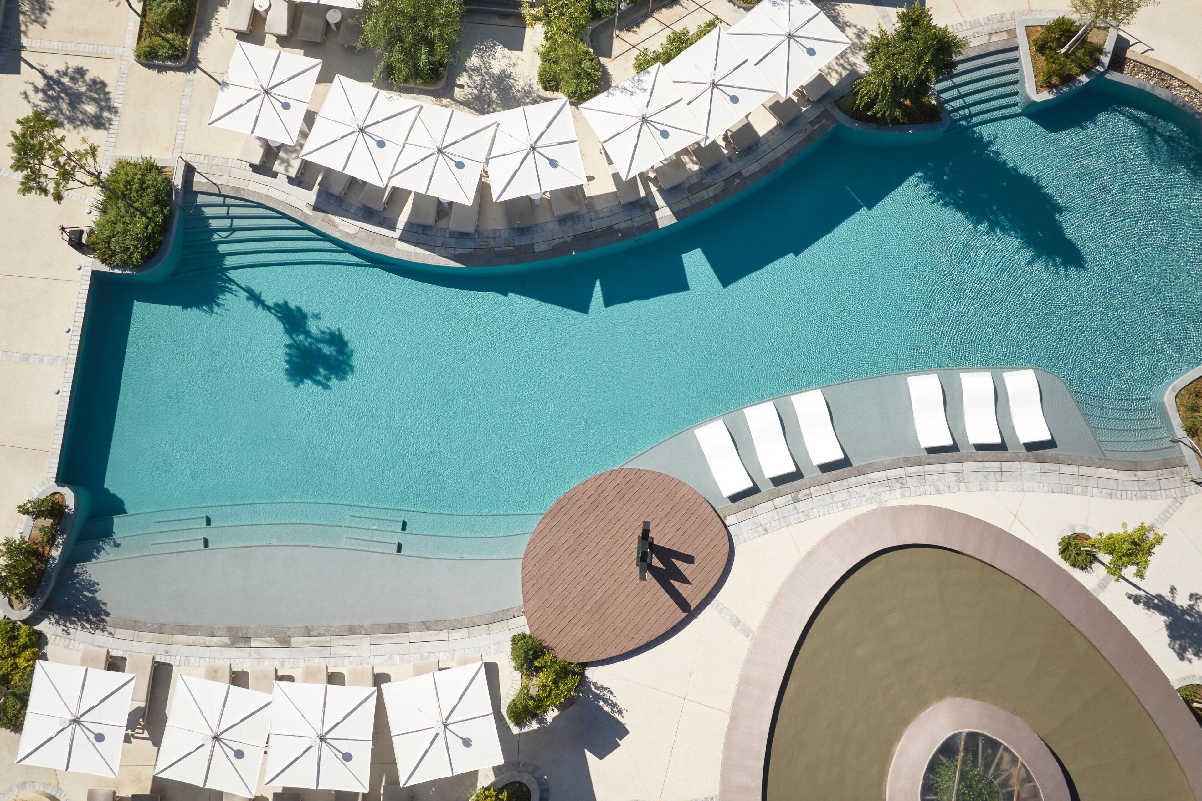 Vista aérea de uma área de piscina com espreguiçadeiras, guarda-sóis e um deck circular.