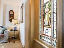 Um quarto aconchegante com sofá, luminária, relógio e uma janela de vitrais.