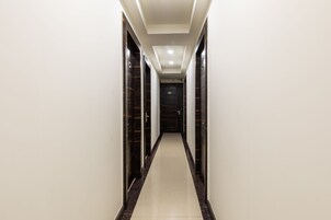 Um corredor estreito e bem iluminado, com portas de madeira escura em ambos os lados e chão de azulejos.
