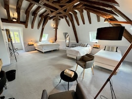 Um amplo quarto no estilo loft, com vigas de madeira aparentes, uma cama grande, um sofá e uma TV.