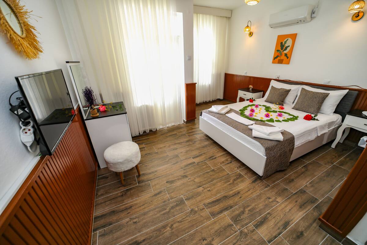 Quarto de hotel com uma cama, uma escrivaninha, uma cadeira, um espelho e uma janela com cortinas.