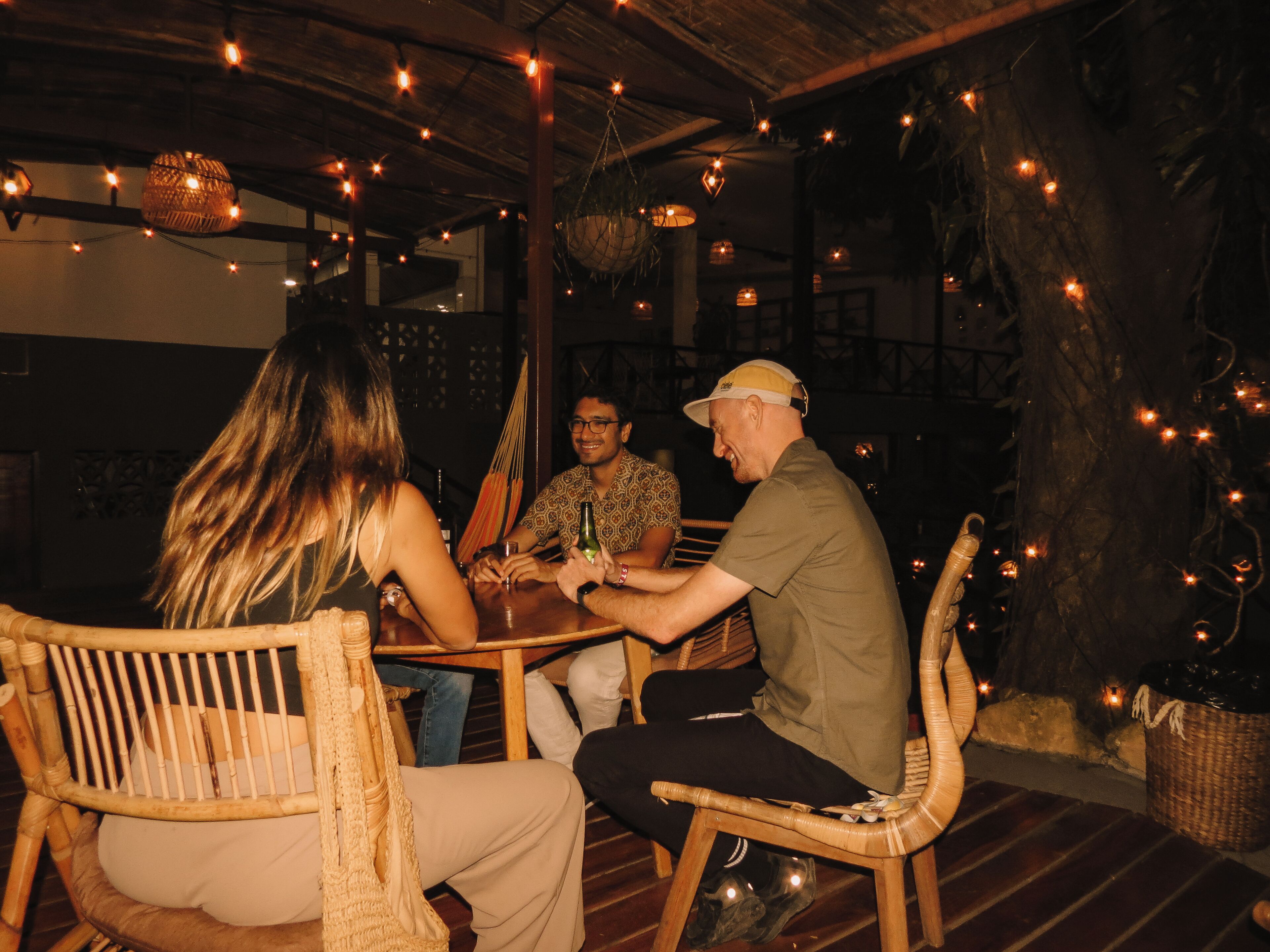 Um grupo de pessoas sentadas numa mesa ao ar livre, com luzes de festa penduradas acima.