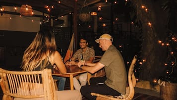 Um grupo de pessoas sentadas numa mesa ao ar livre, com luzes de festa penduradas acima.