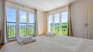 Quarto de hotel com uma cama grande, uma varanda com vista para o verde e uma porta à direita.
