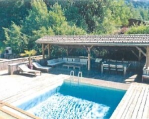 Piscina com deck de madeira e área de descanso, cercada por árvores.