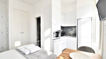 Quarto de hotel moderno com cama, uma mesa de madeira, área de cozinha com micro-ondas e televisão.