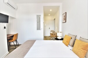 Quarto de hotel com uma cama, uma escrivaninha, uma cadeira e uma luminária.