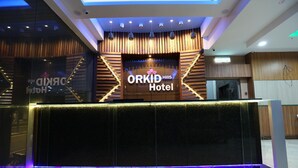 Uma área de recepção com design moderno, destacando um balcão de madeira e uma placa com a inscrição "ORKID HILLS Hotel".