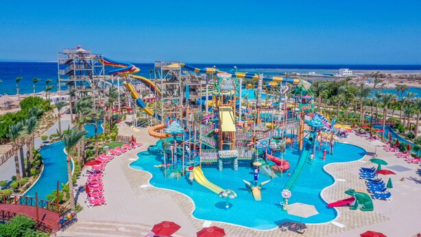 Parque aquático com vários toboáguas e piscinas, cercado por palmeiras e vista para a praia.