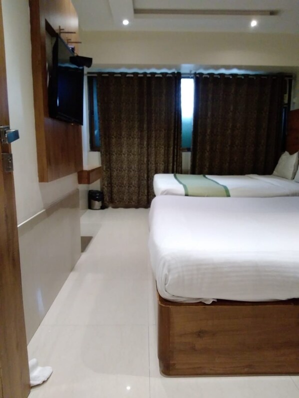 Quarto de hotel com uma cama, televisão na parede e janela com cortinas.