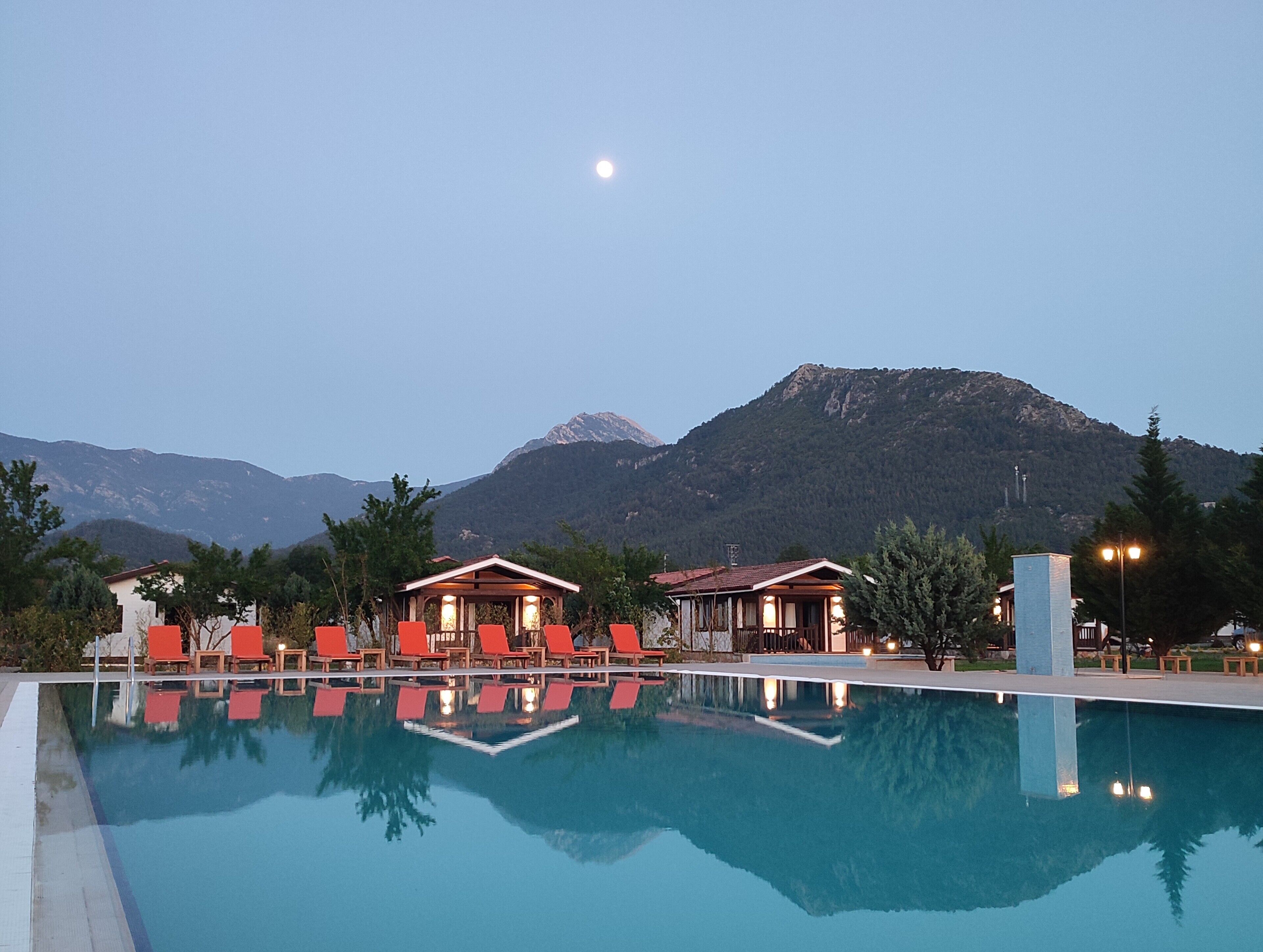 Piscina com espreguiçadeiras e montanhas ao fundo.