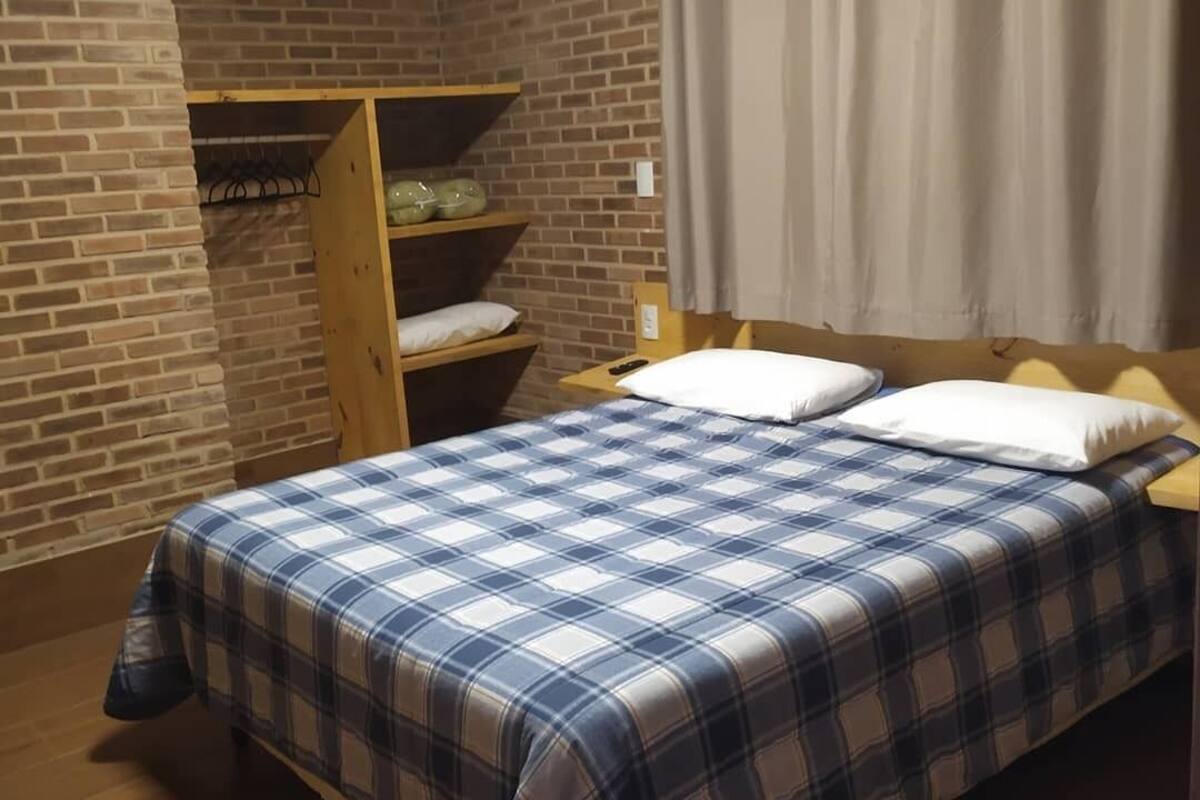 Quarto com cama, guarda-roupa de madeira e parede de tijolos.