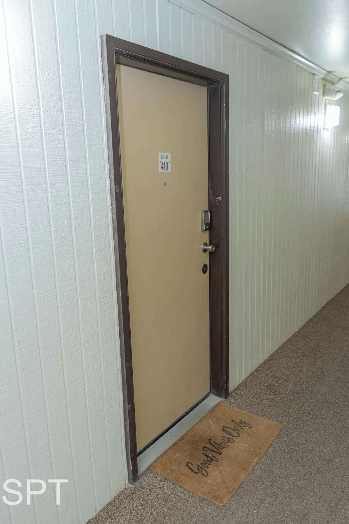 Uma porta bege com moldura marrom, um interfone e um tapete de entrada com um nome.