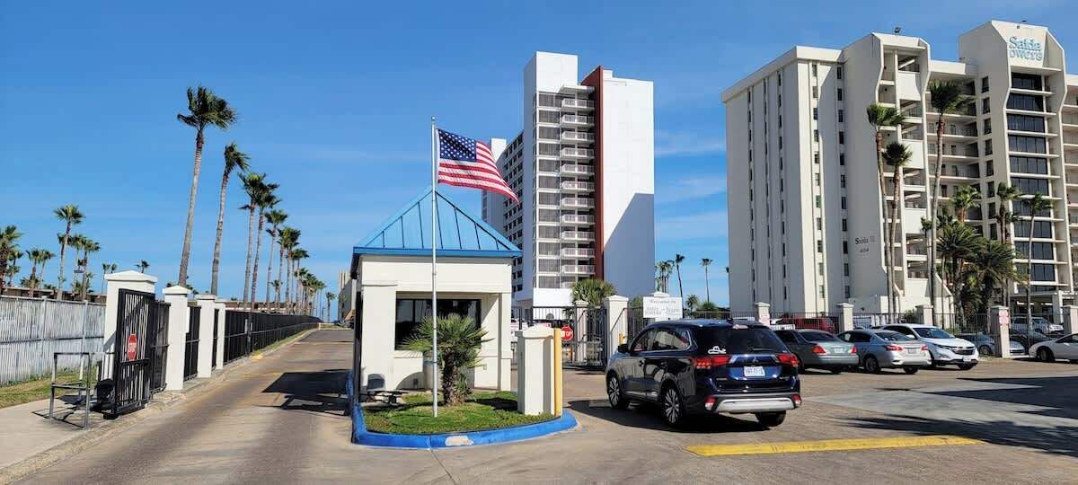 Entrada de hotel com uma bandeira, estacionamento e edifícios altos ao fundo.