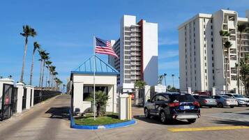 Entrada de hotel com uma bandeira, estacionamento e edifícios altos ao fundo.
