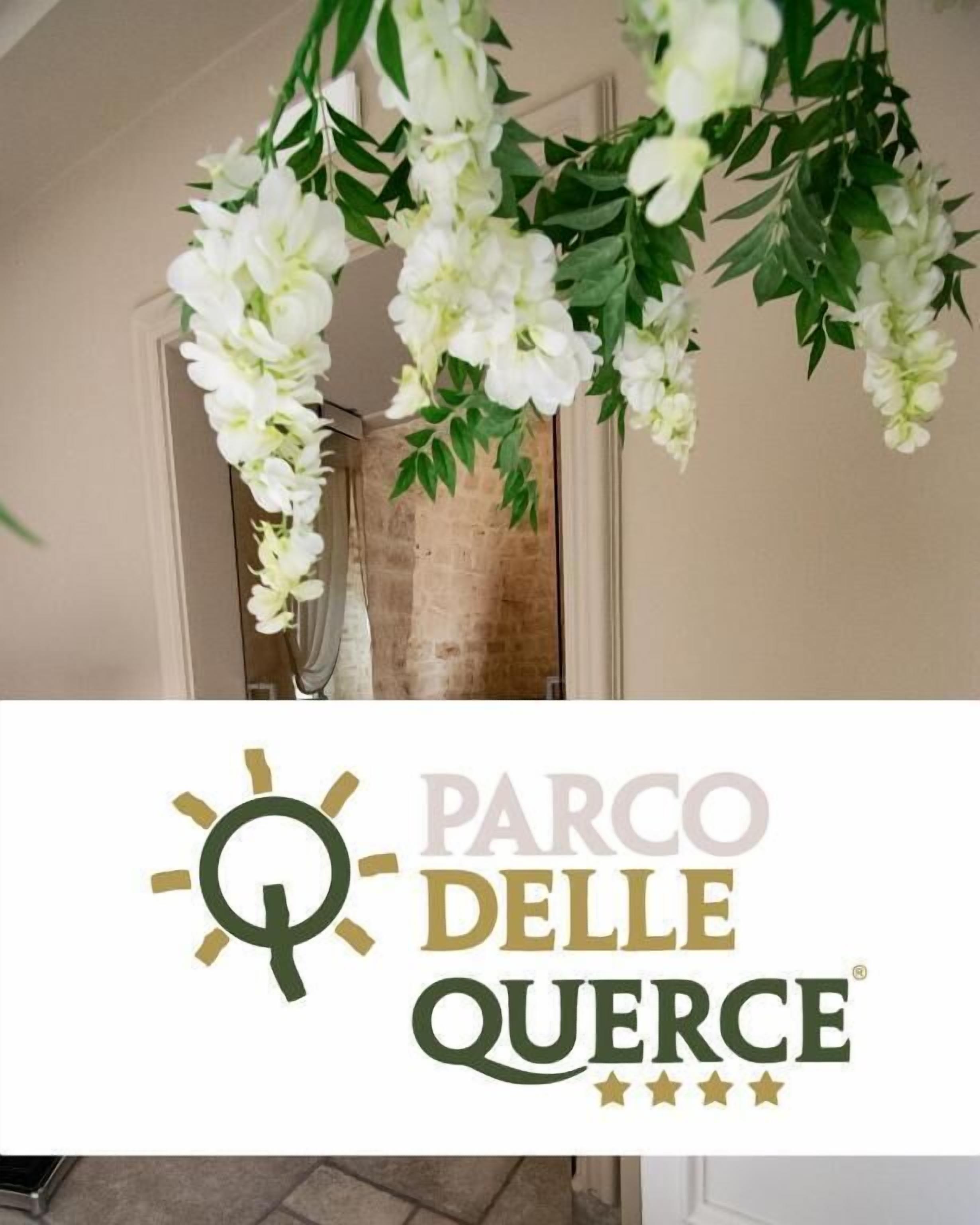 Um corredor com um arranjo floral branco decorativo e o logotipo de "PARCO DELLE QUERCE" com um símbolo de sol e quatro estrelas.