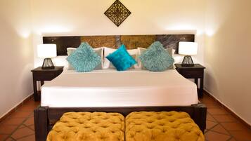 Quarto de hotel com uma cama grande, duas luminárias de cabeceira, almofadas decorativas, ar condicionado fixado na parede e piso estampado.