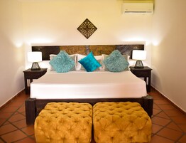Quarto de hotel com uma cama grande, duas luminárias de cabeceira, almofadas decorativas, ar condicionado fixado na parede e piso estampado.