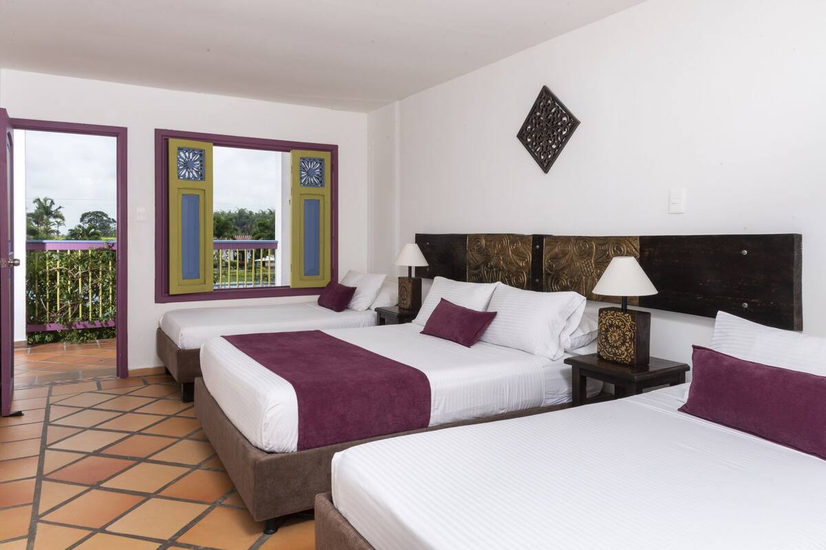 Quarto de hotel com três camas, varanda e um objeto decorativo na parede.