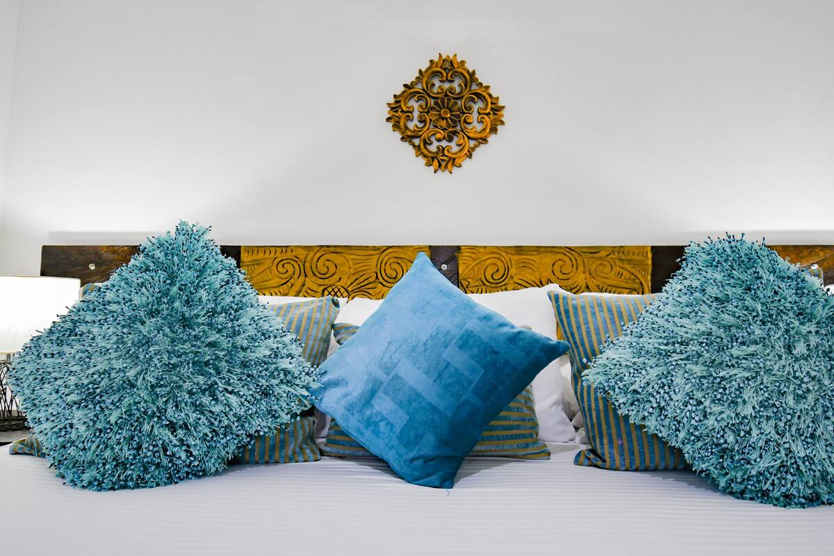 Cama com cabeceira, várias almofadas e um objeto decorativo na parede.