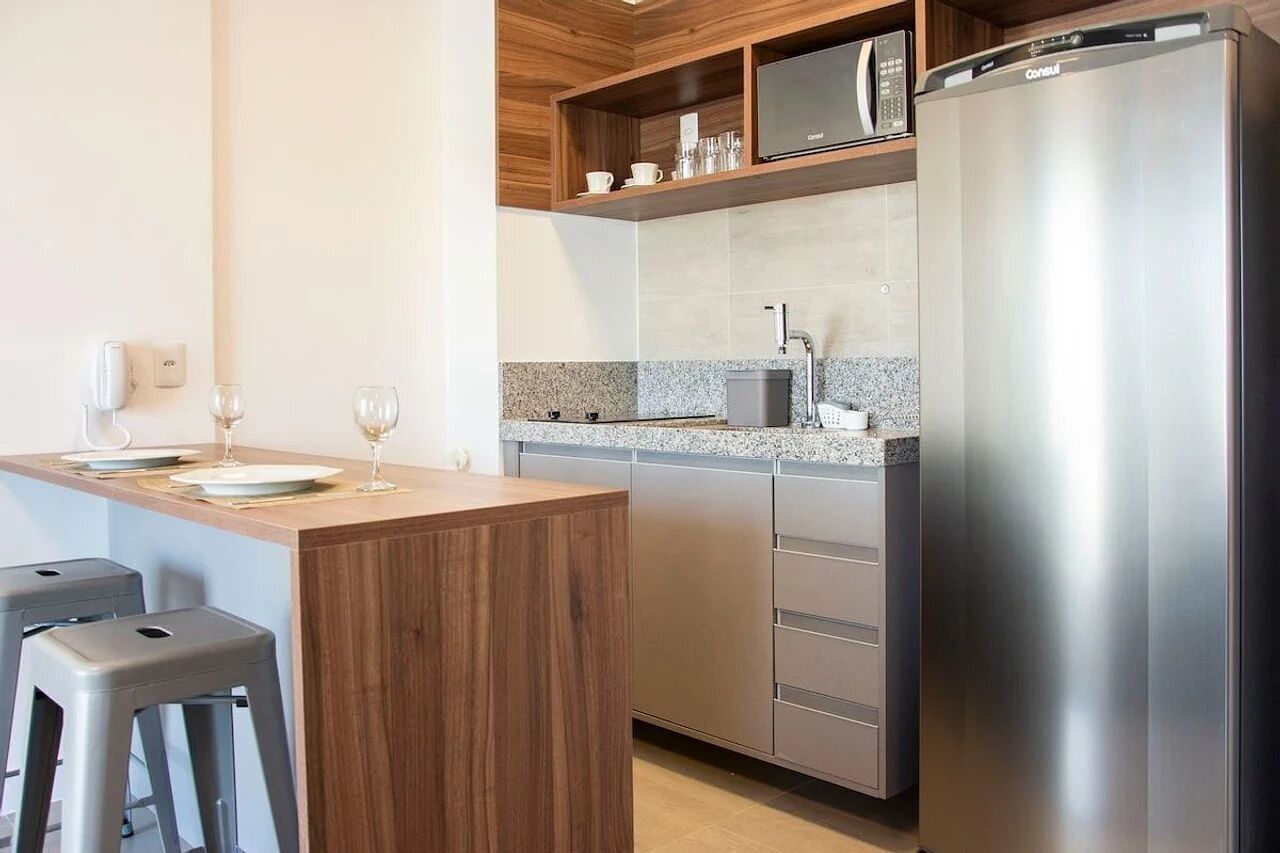 Uma cozinha moderna com geladeira de aço inoxidável, bancada de granito, armários de madeira e banquetas de bar.