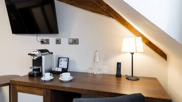 Quarto de hotel com secretária de madeira, televisão de tela plana na parede, cafeteira, luminária e telefone.