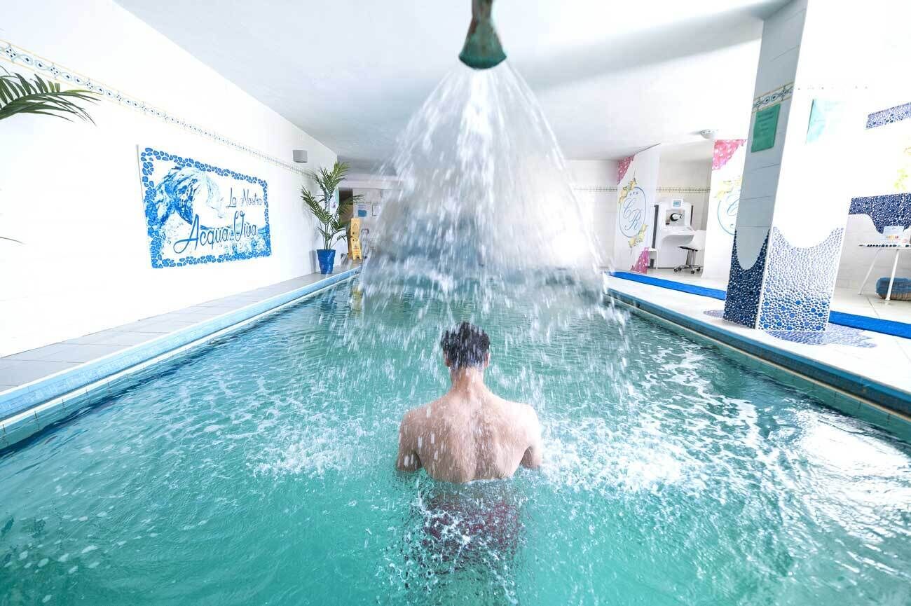 Um homem em uma piscina com jatos d'água saindo do teto.