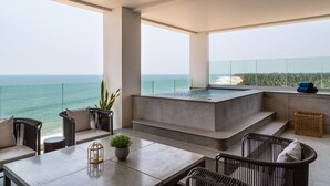 Uma varanda com vista para o oceano, uma banheira de hidromassagem, móveis de vime e uma pequena mesa com uma planta.
