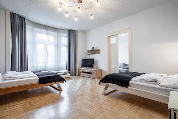 Quarto de hotel moderno com duas camas de solteiro, uma televisão e um chão de madeira em padrão losango.