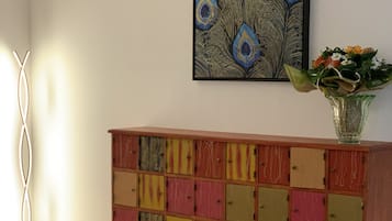 Um quarto com uma poltrona verde, um armário colorido, uma pintura com tema de pavão e um vaso com flores.