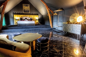 Quarto moderno com cama, área de estar com mesa e banquinho, guarda-roupa e um espelho grande.