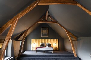 Quarto com teto inclinado, cama com almofadas, cabeceira e duas luminárias de apoio.