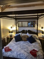 Uma cama com dossel com um espelho acima, duas mesas de cabeceira com luminárias e uma meia vermelha sobre a cama.