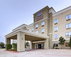 Um hotel Comfort Suites com entrada coberta, vários andares e céu claro.