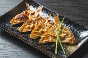 Prato de peixe frito com guarnição verde sobre um prato escuro.