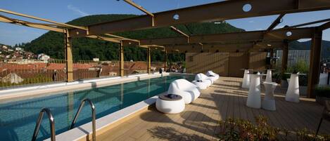 Uma área à beira da piscina com deck de madeira, espreguiçadeiras e piscina.