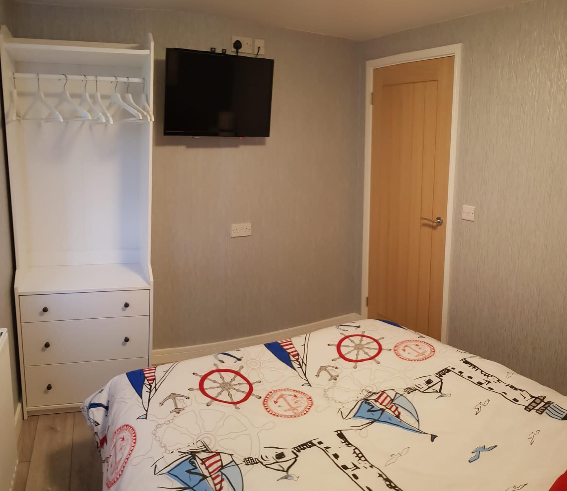 Um quarto com uma cama, um guarda-roupa, uma televisão e uma porta.