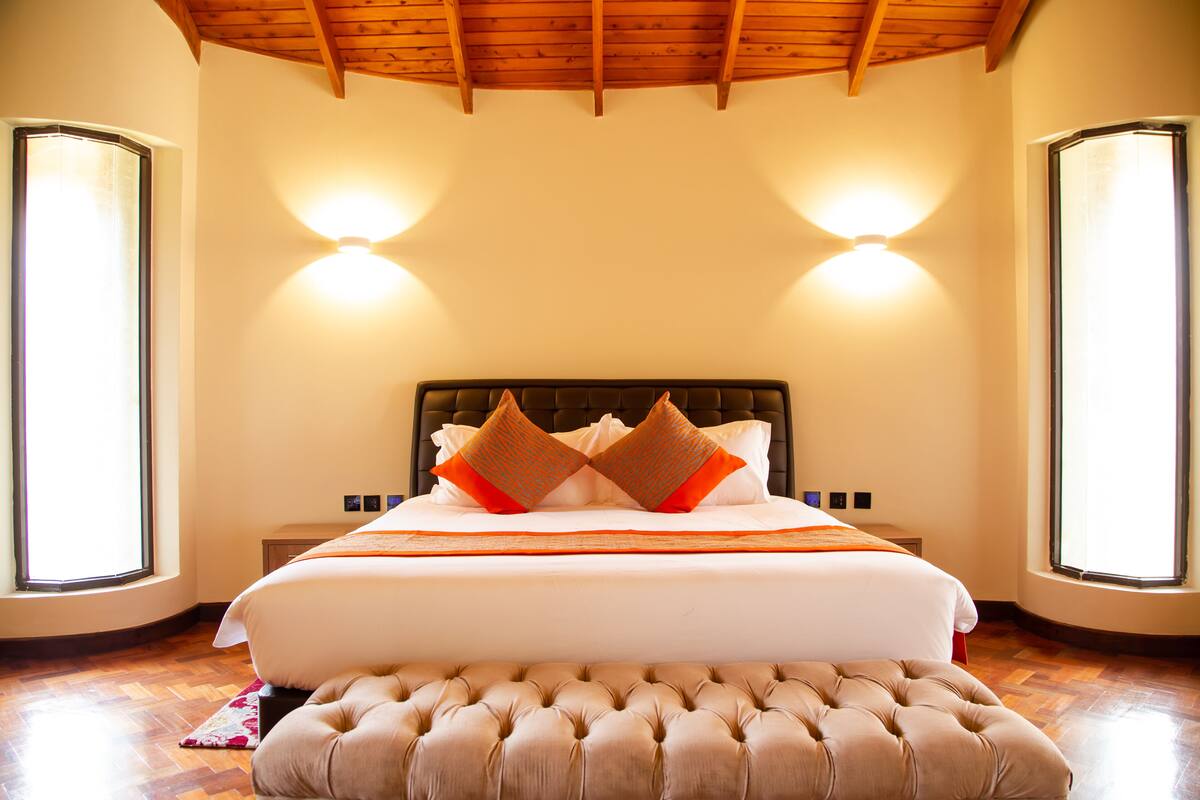 Quarto bem arrumado com uma cama grande, duas luzes fixadas na parede e uma janela de um lado.