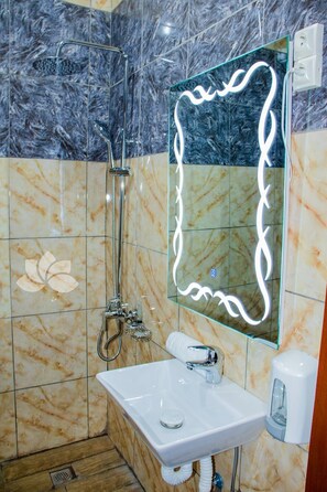 Um banheiro com chuveiro, pia e espelho com moldura decorativa.