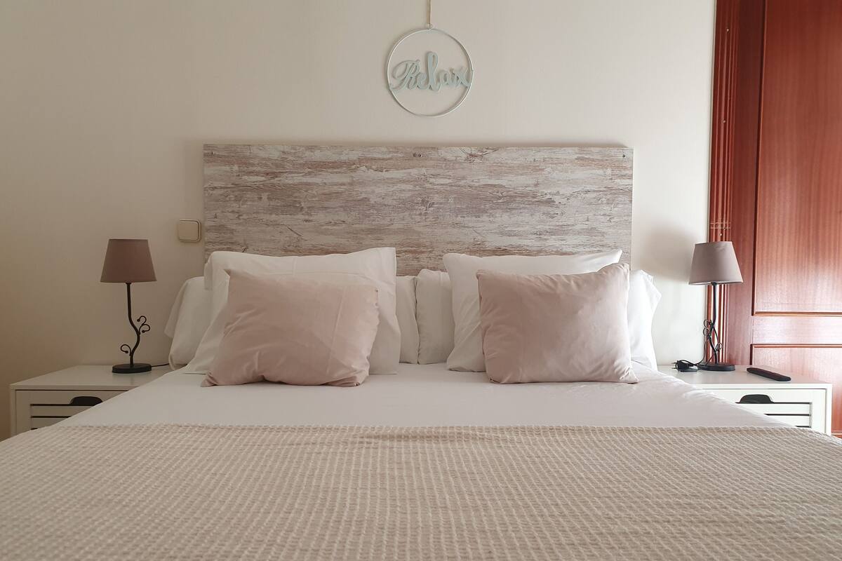 Cama bem arrumada com duas almofadas, um cobertor texturizado e uma placa fixada na parede acima.