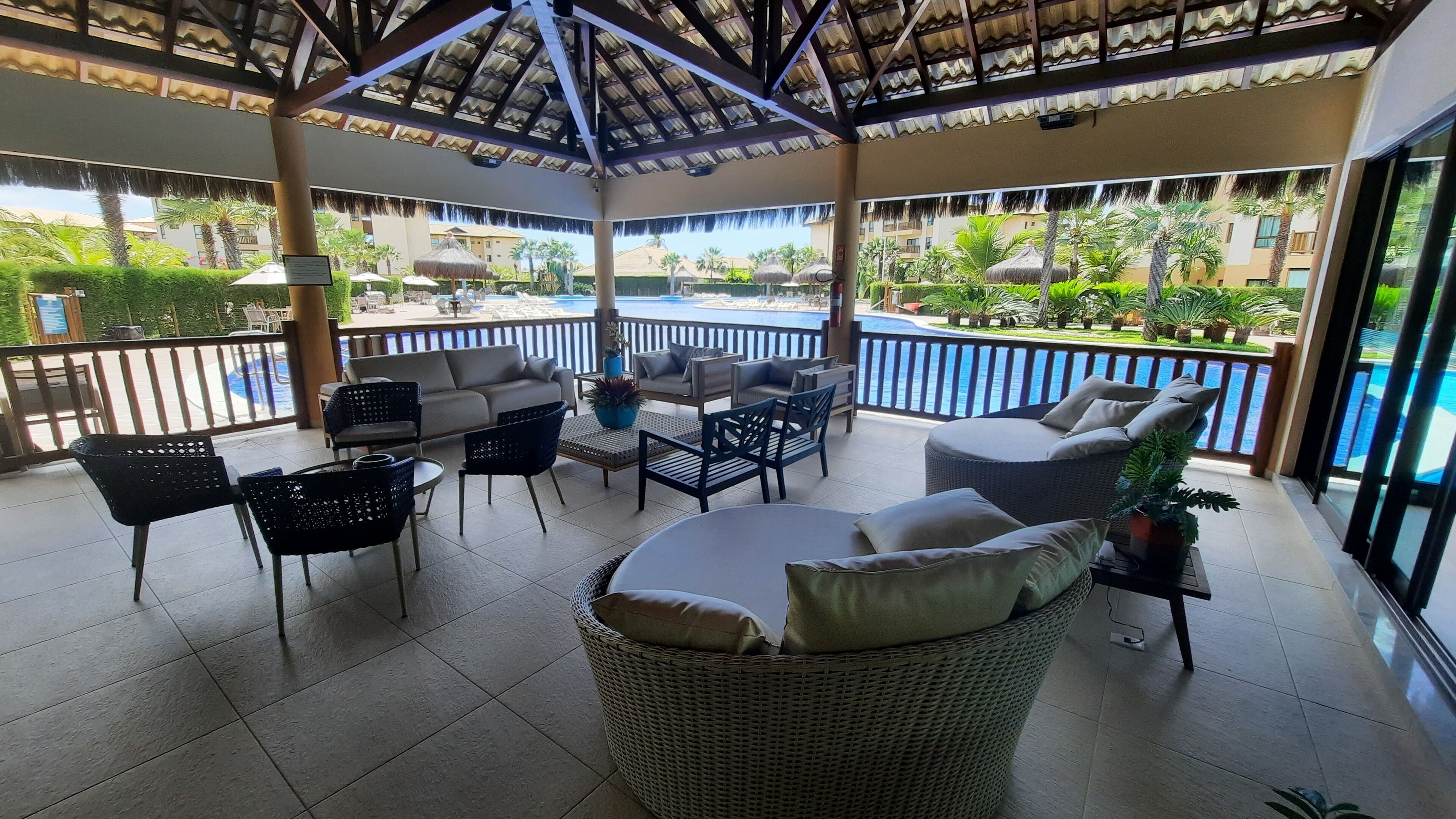 Uma área de estar coberta ao ar livre, com móveis de vime e vista para uma piscina.