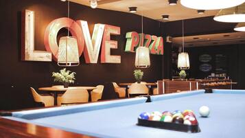 Uma mesa de bilhar com bolas de bilhar, uma mesa de sinuca e uma parede com letras iluminadas que formam a frase 'LOVE PIZZA'.