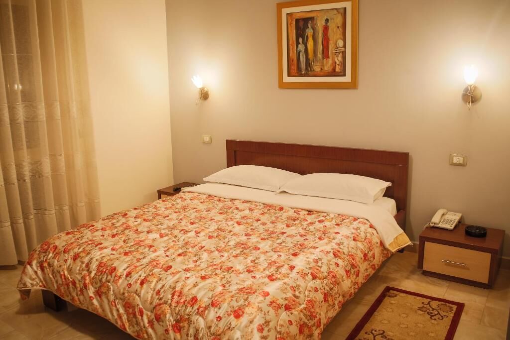 Quarto de hotel com uma cama, uma mesa de cabeceira com telefone, um quadro na parede e uma cortina.