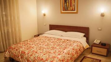 Quarto de hotel com uma cama, uma mesa de cabeceira com telefone, um quadro na parede e uma cortina.