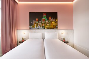 Quarto de hotel com duas camas, vista noturna de um horizonte urbano e um quadro pendurado na parede.