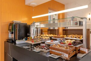 Buffet com diversos produtos de pastelaria, máquina de café e posto de atendimento automático.