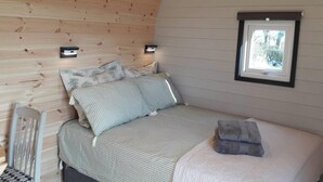 Um quarto aconchegante com cama, travesseiros, uma pequena janela e mesa de cabeceira.