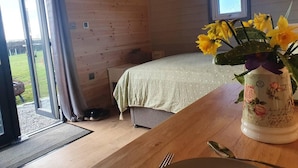 Um quarto aconchegante com uma cama, uma janela pequena e um vaso com flores sobre uma mesa.