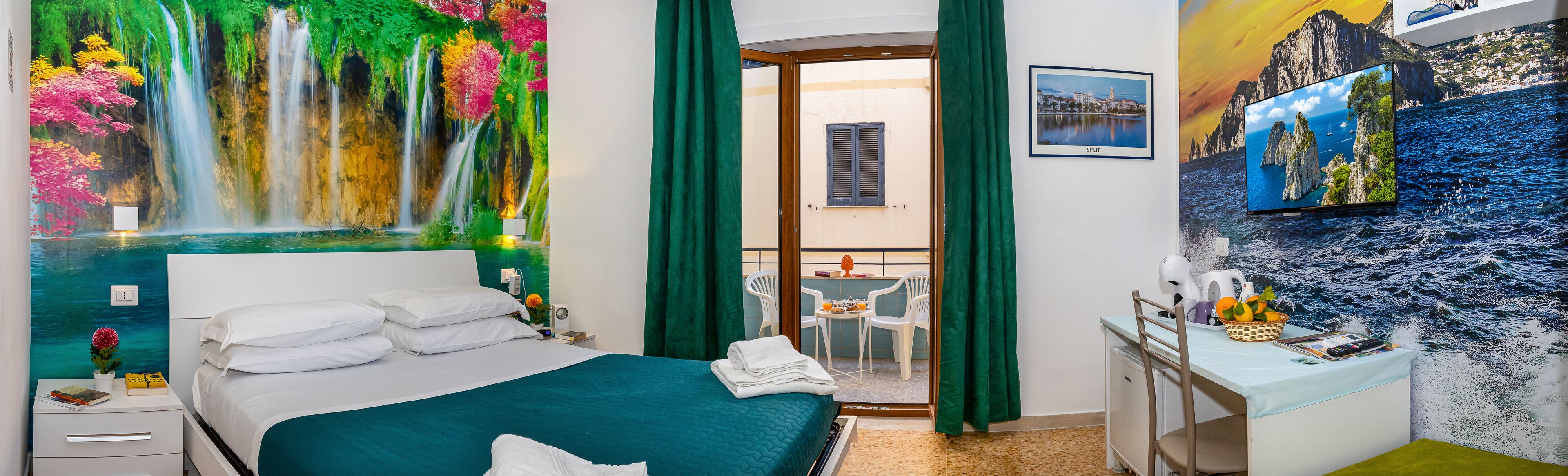 Quarto de hotel com cama, escrivaninha, cadeira, mesa pequena e varanda com vista.