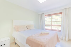 Quarto com cama, mesa de cabeceira e janela com cortinas.